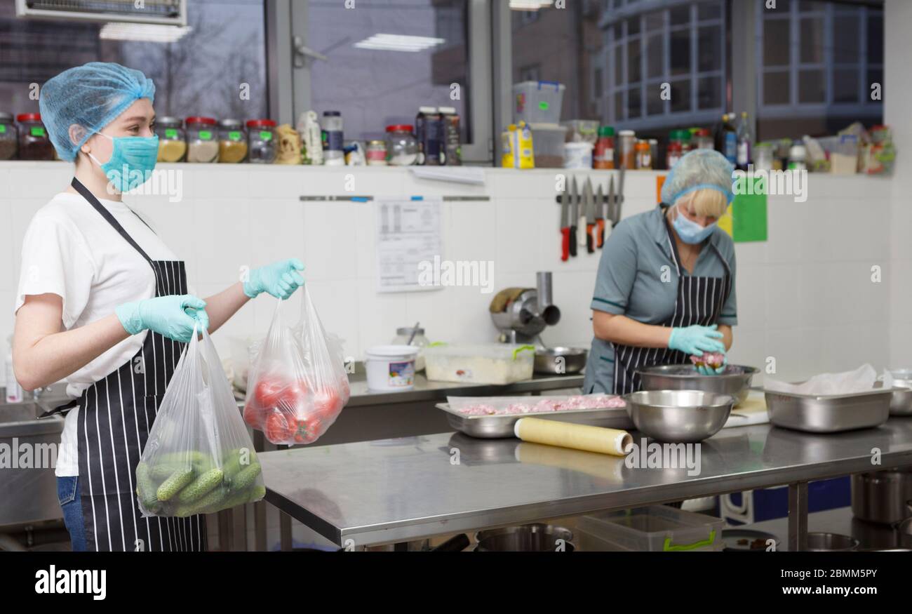 Kitchen workers cooking of fresh ingredients and wearing protective ...