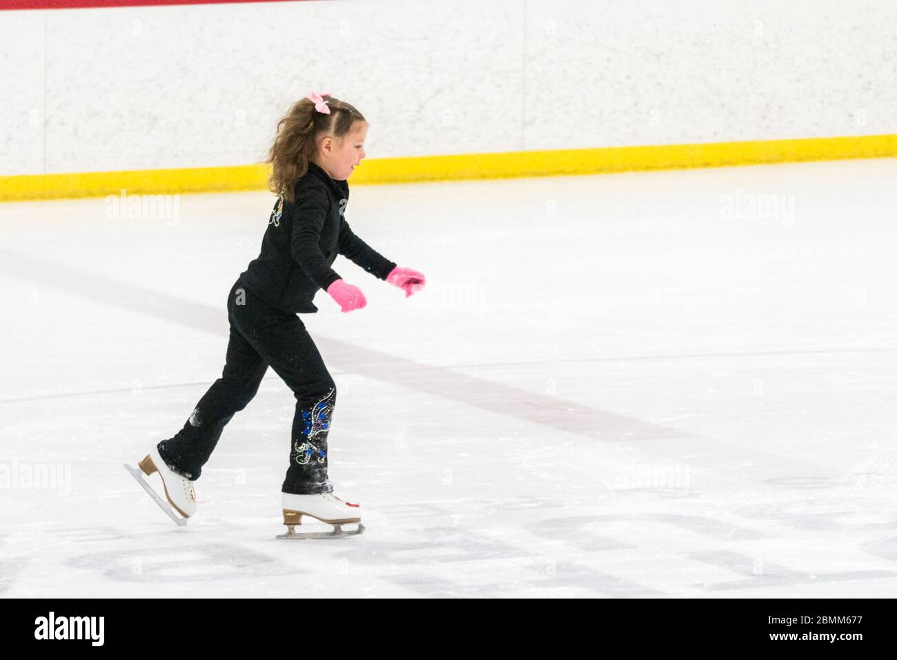 Little girl practicing figure skating moves on the indoor ice rink ...