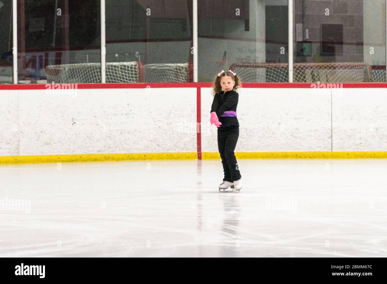 Little girl practicing figure skating moves on the indoor ice rink ...