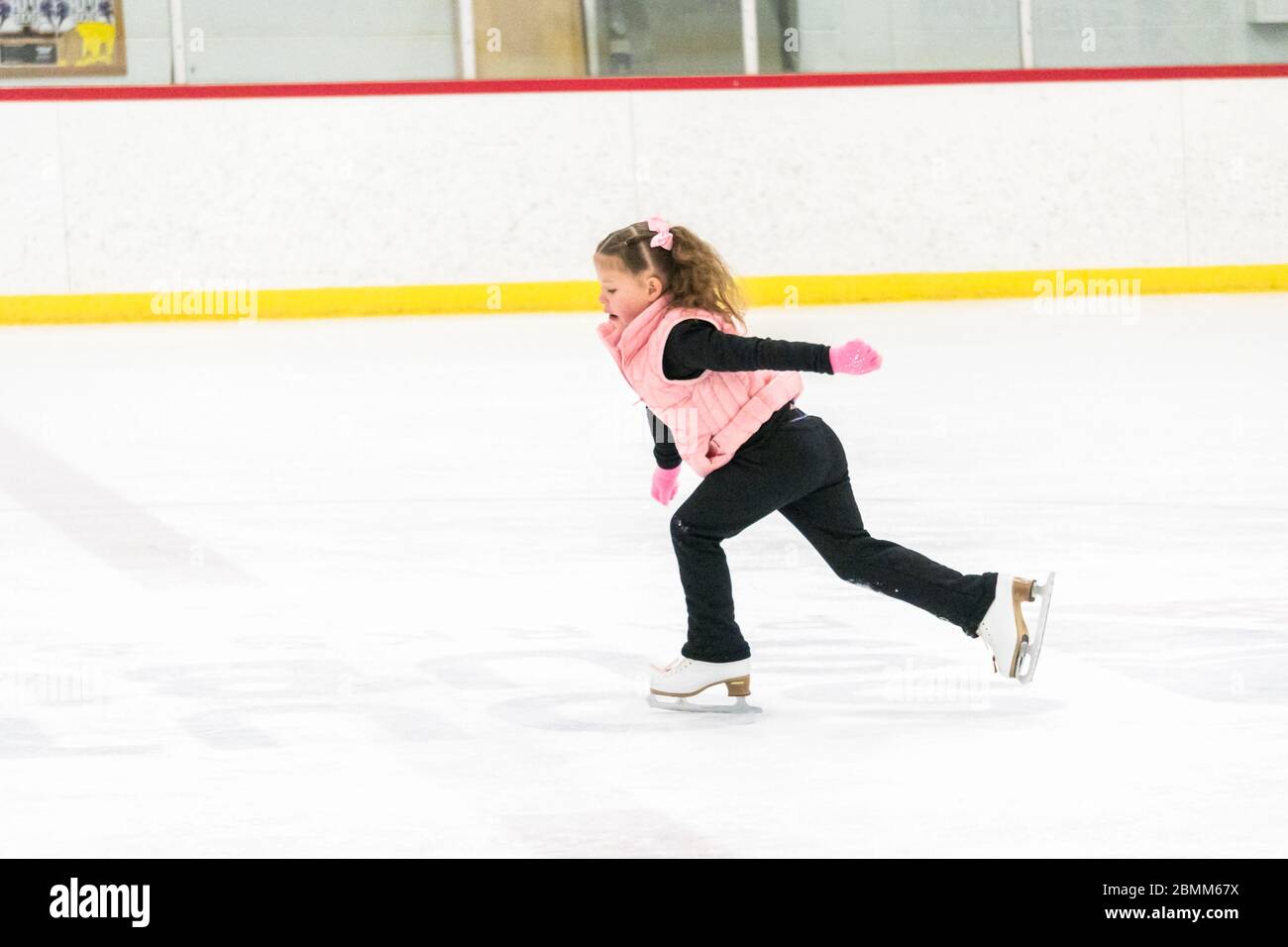 Little girl practicing figure skating moves on the indoor ice rink ...