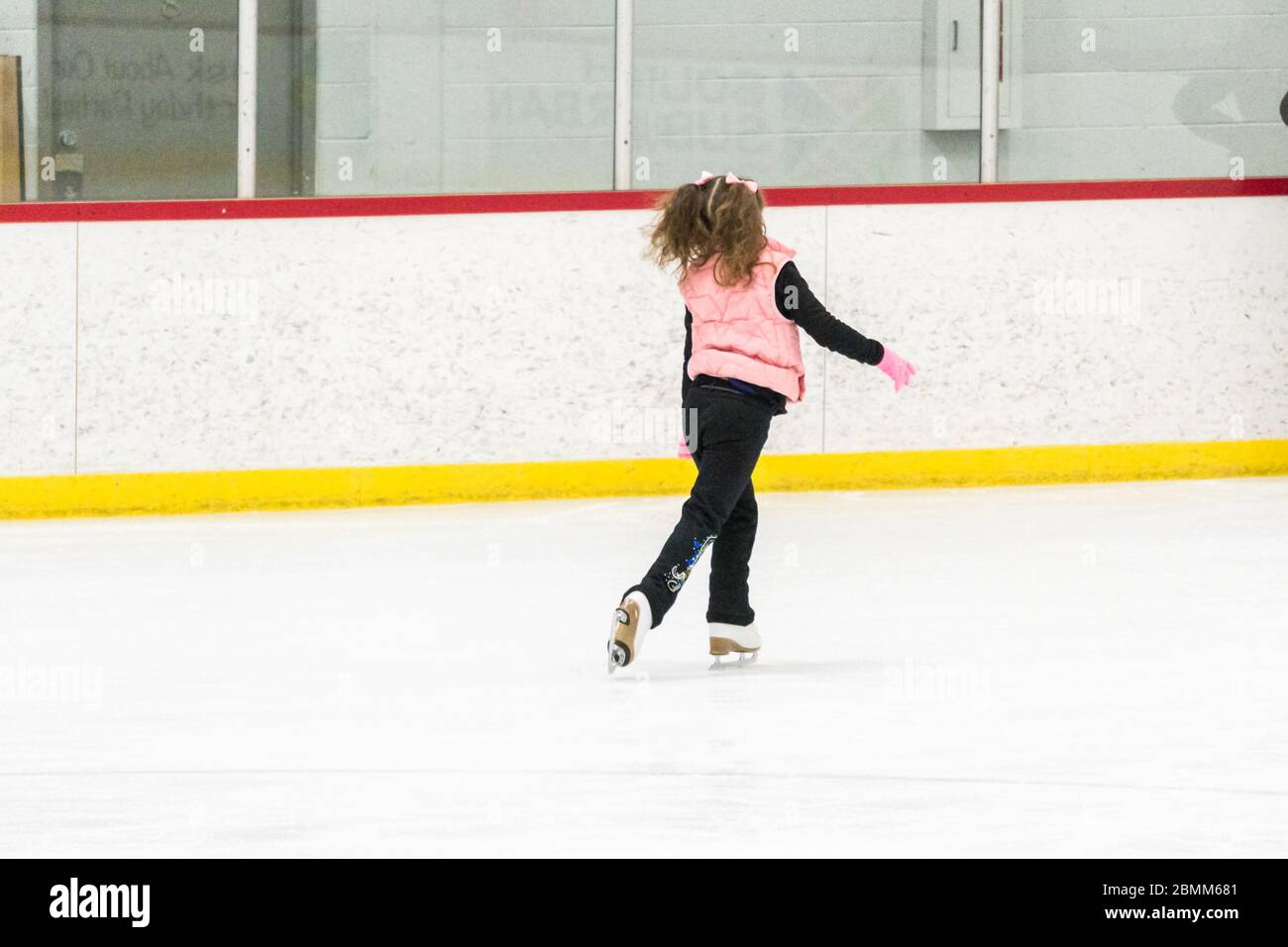 Little girl practicing figure skating moves on the indoor ice rink ...