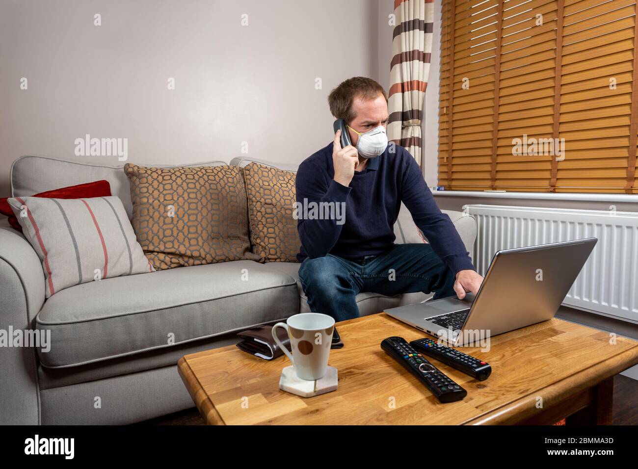Man struggling working from home at a coffee table wearing a face mask ...