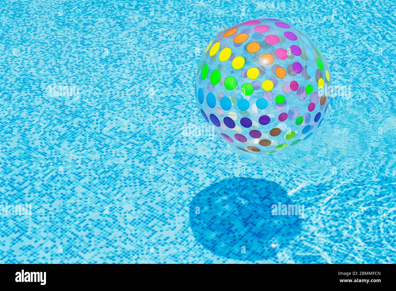 Inflatable colourful ball floating in blue swimming pool water with ...