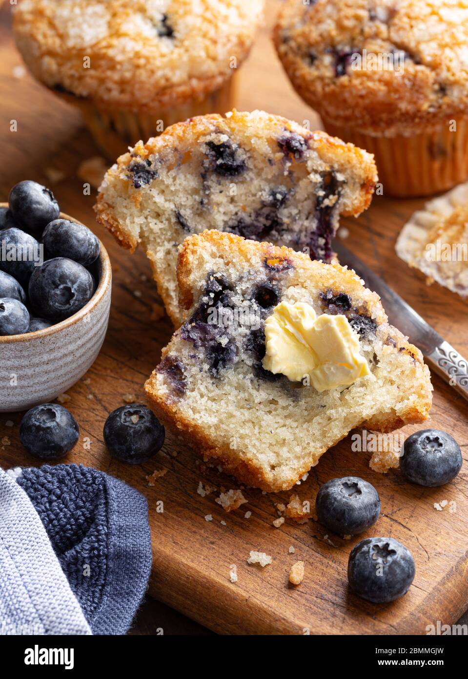 Blueberry muffin cut in half with butter and fresh berries on a rustic ...