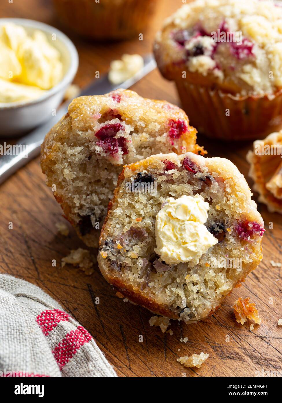 Closeup of a blueberry and cranberry muffin cut in half with butter on ...