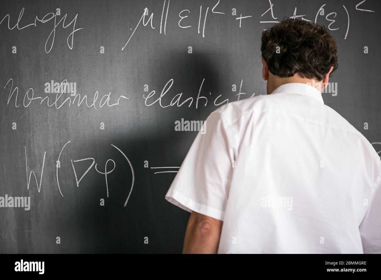 Senior math teacher teaching mathematics, writing on the blackboard ...