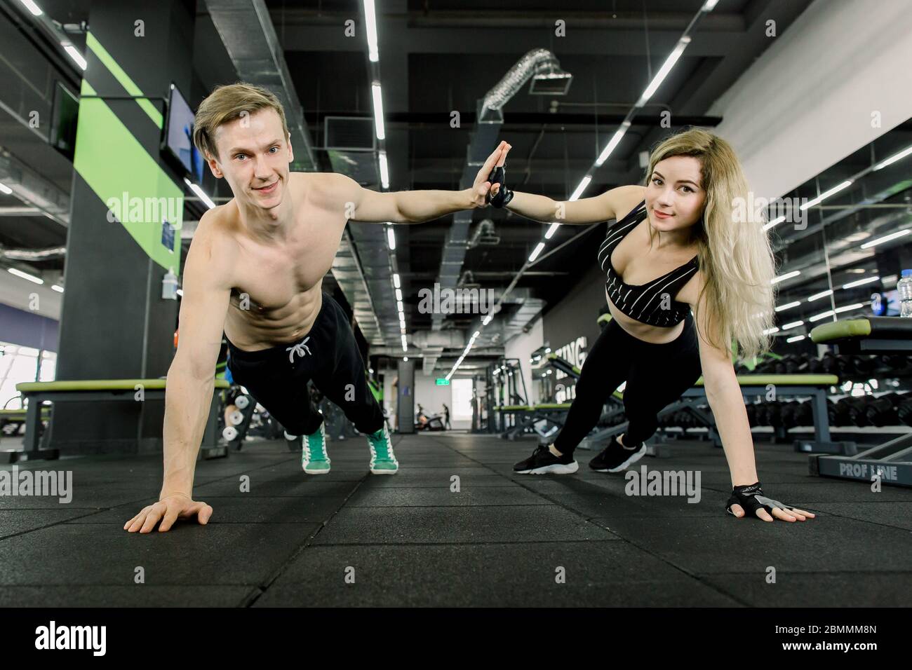 Couple doing pushups at training in gym. Sporty couple doing push-ups and giving high five. Gym ...