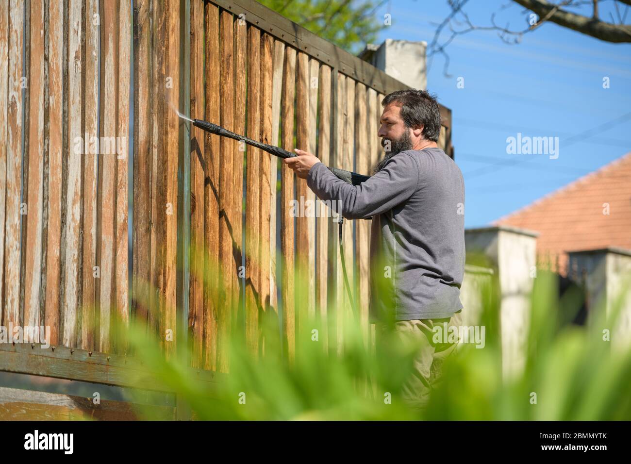 Mid adult man cleaning a wooden gate with a power washer. High water ...