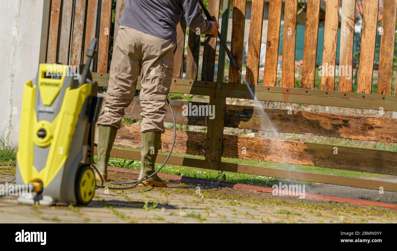 Unrecognizable man cleaning a wooden gate with a power washer. High ...