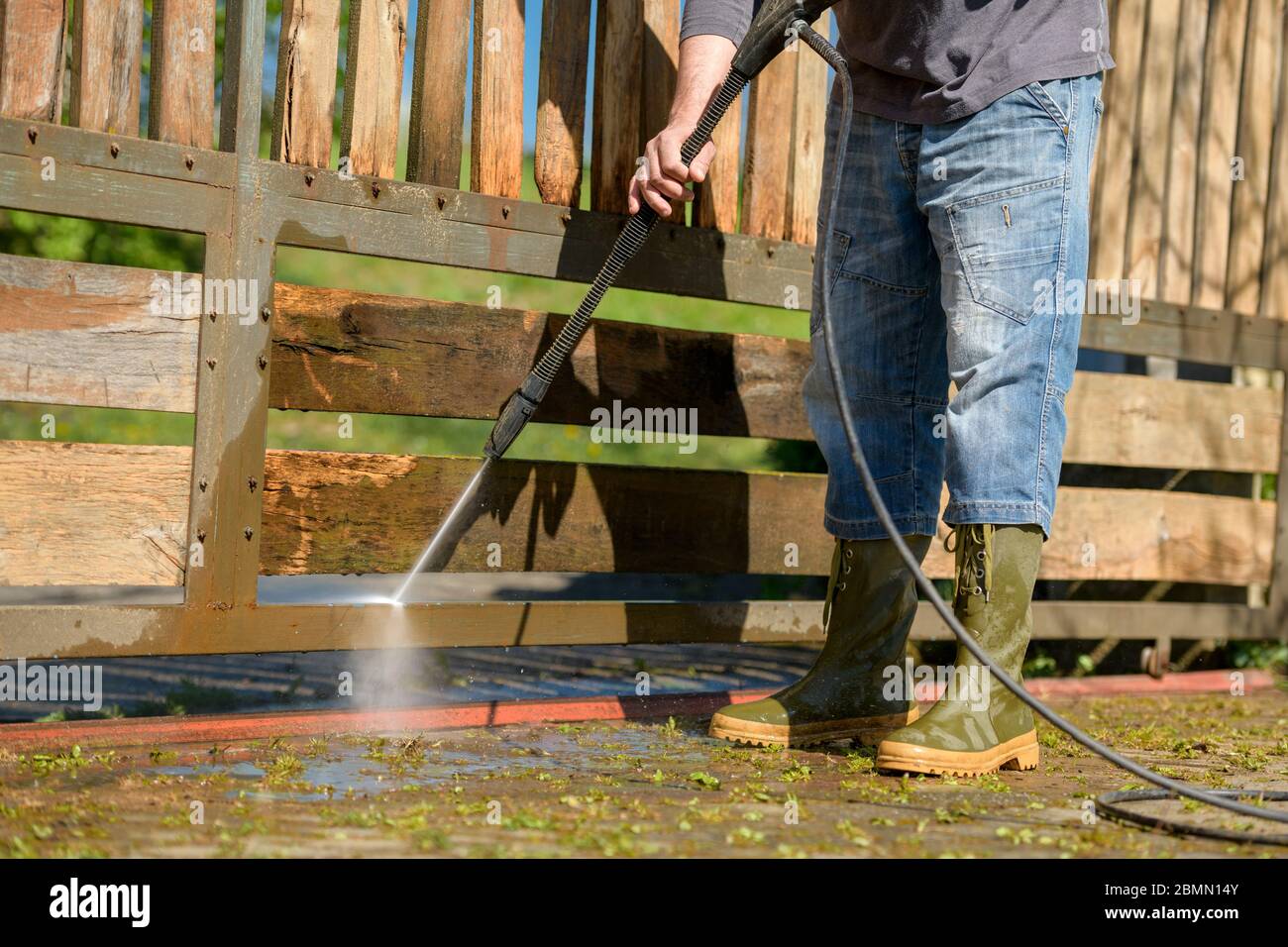 Unrecognizable man cleaning a wooden gate with a power washer. High ...