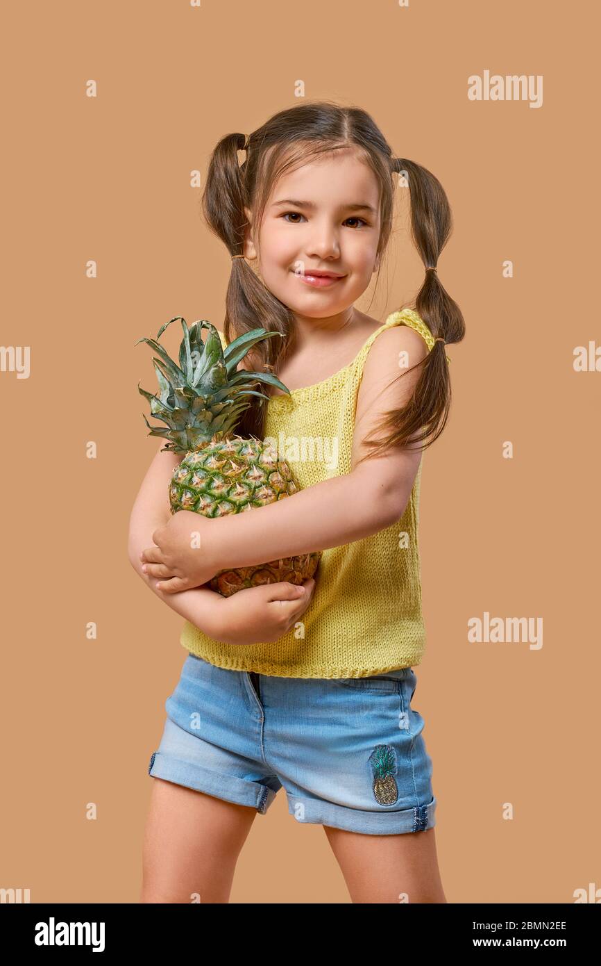 Funny young girl playfully posing with pineapple on beige background ...
