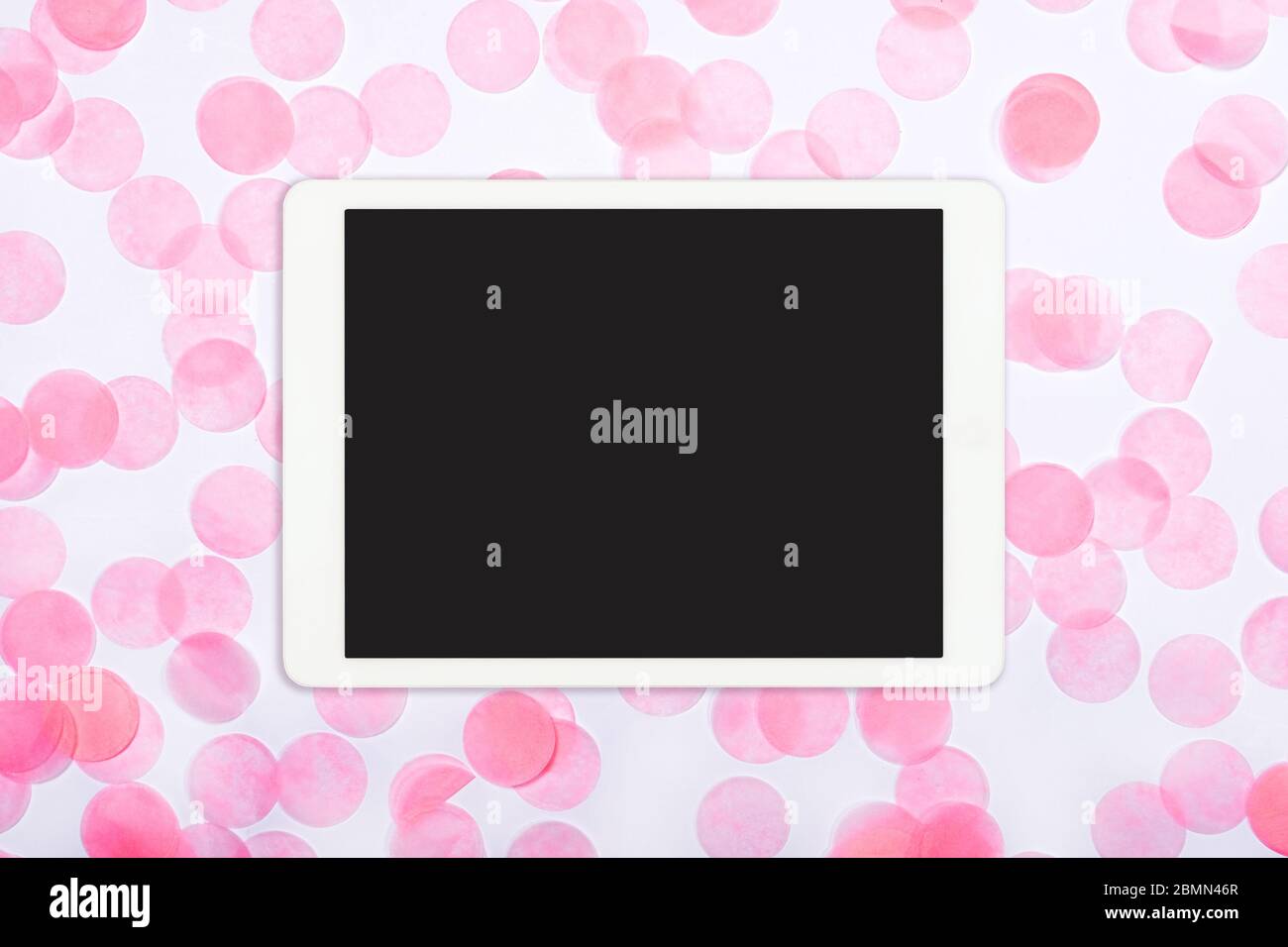 Flat lay of white touchpad with blank screen on pink confetti ...