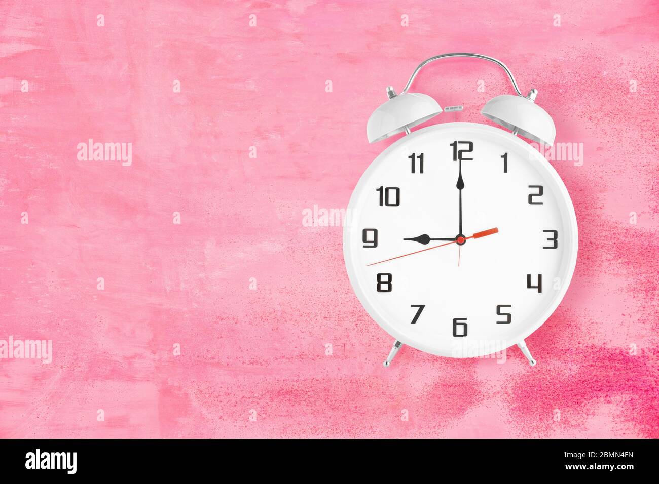 Alarm clock with twin bells and ringer showing 9 nine o'clock on pink ...