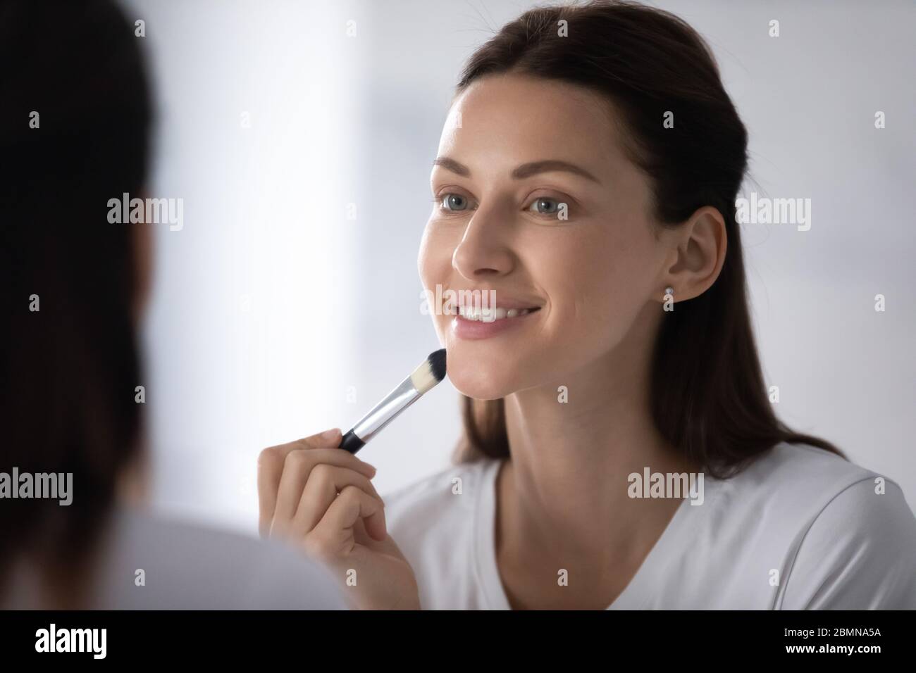 Beautiful woman using makeup brush applying concealer foundation cream ...