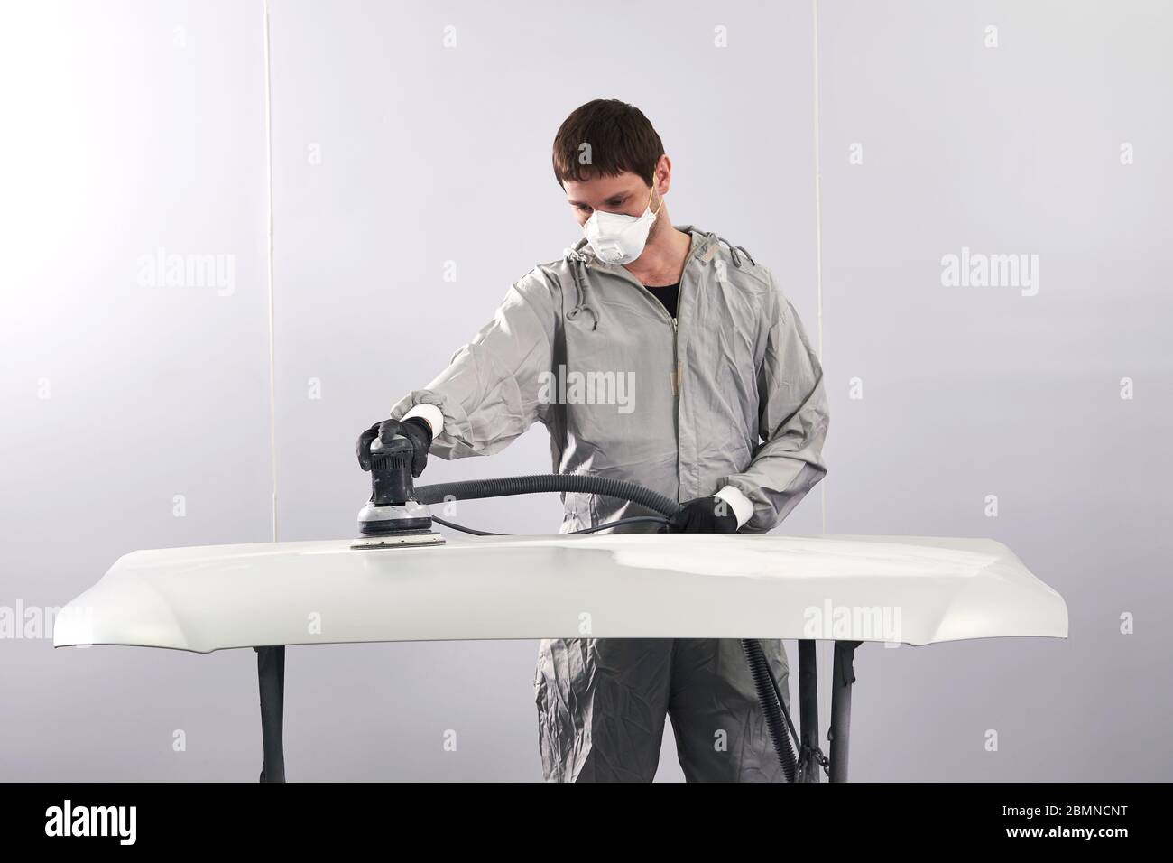 Auto mechanic wearing face mask buffing and polishing car hood in auto ...