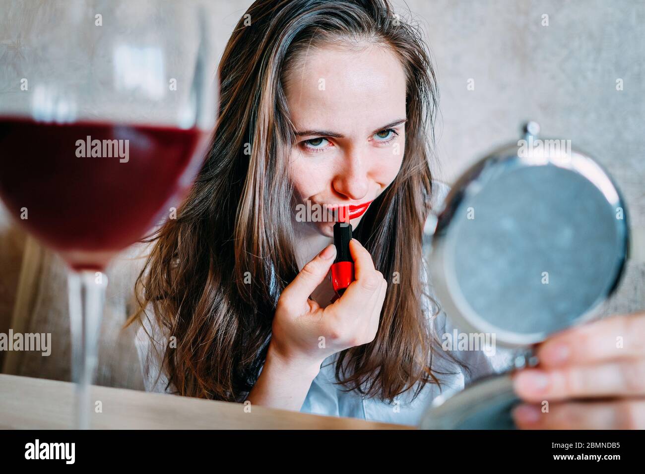 Drunk girl with a glass of wine paints her lips with red lipstick ...