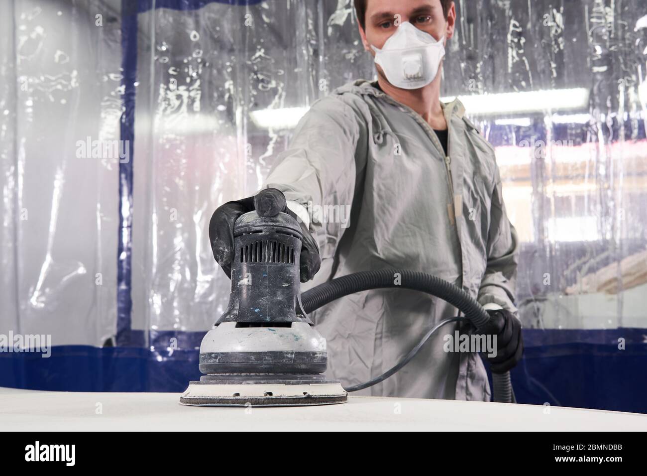 Auto mechanic wearing face mask buffing and polishing car hood in auto ...