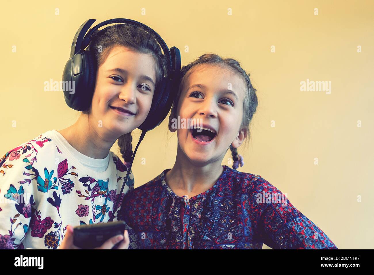 Two little happy girls together listening to music. toned Stock Photo ...