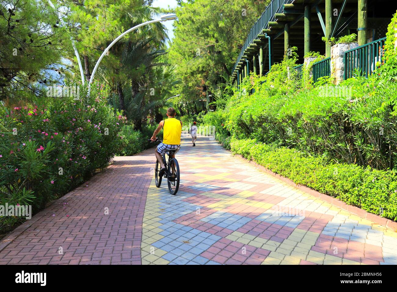 A teenager rides a bicycle along a bike path in a park in a resort town ...