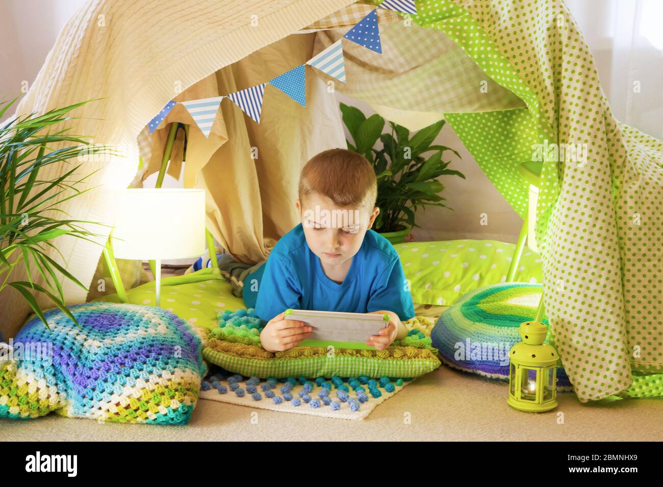 Cute boy, playing on tablet and telephone in campside, in the tent ...