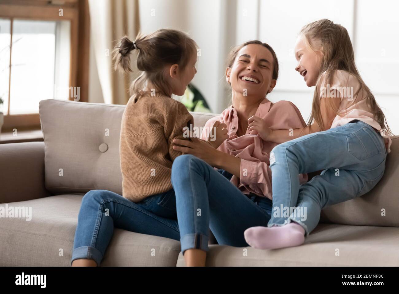 Happy mother playing with little daughters, tickling on couch Stock ...