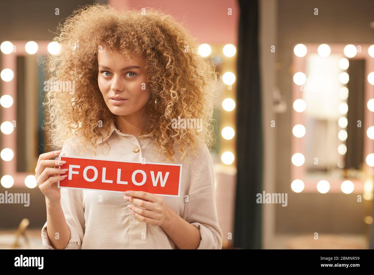 Waist up portrait of modern young woman holding FOLLOW sign while ...
