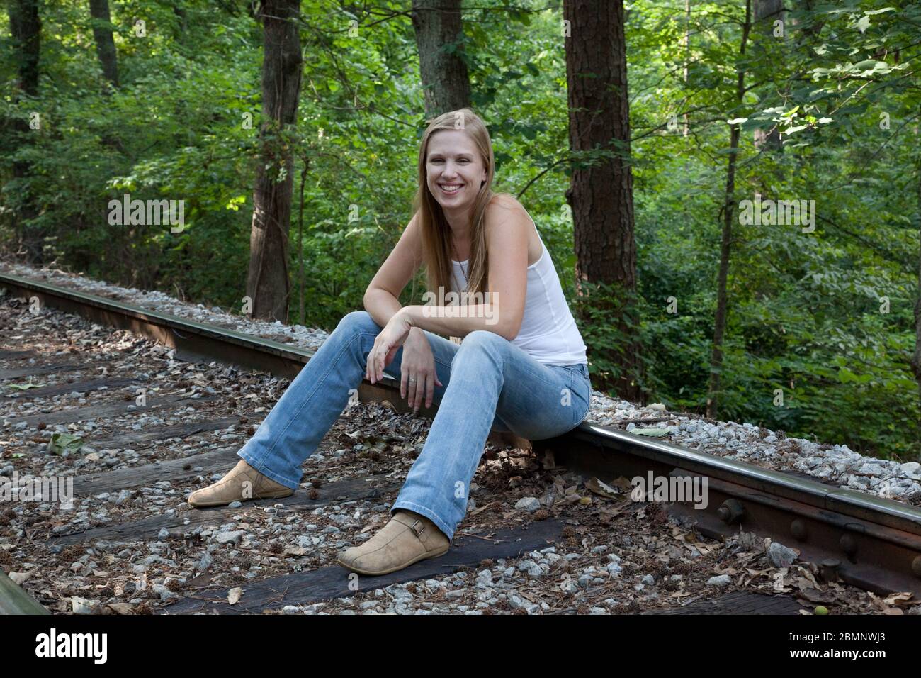 Pretty Blond sitting on Railroad Tracks with a smile Stock Photo - Alamy