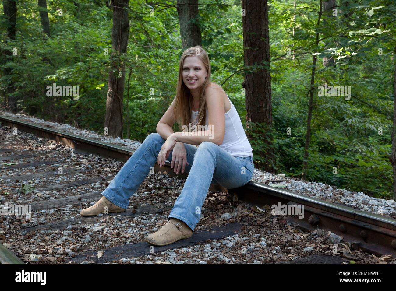 Pretty Blond sitting on Railroad Tracks with a smile Stock Photo - Alamy