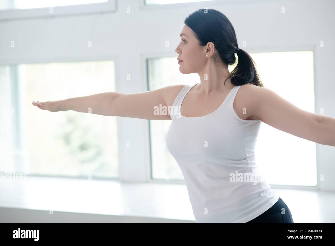 Brunette female standing in warrior pose with arms parallel to the ...