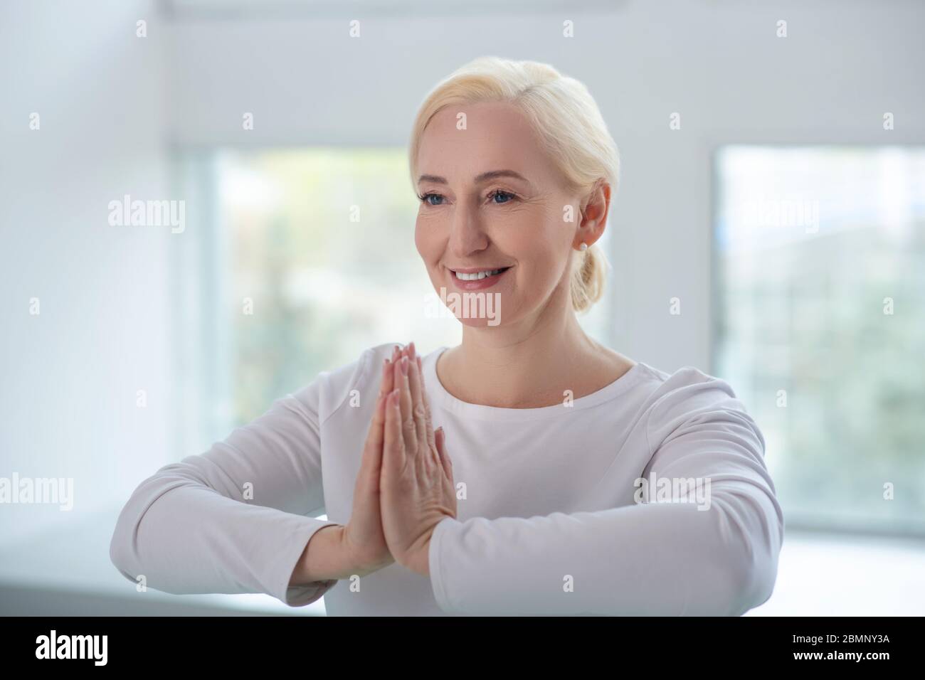 Mature blonde female performing namaste, pressing hands together ...