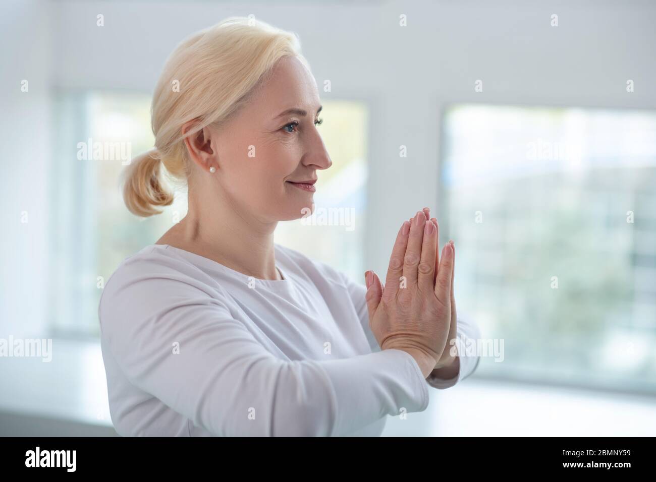 Mature blonde female performing namaste, pressing hands together Stock ...