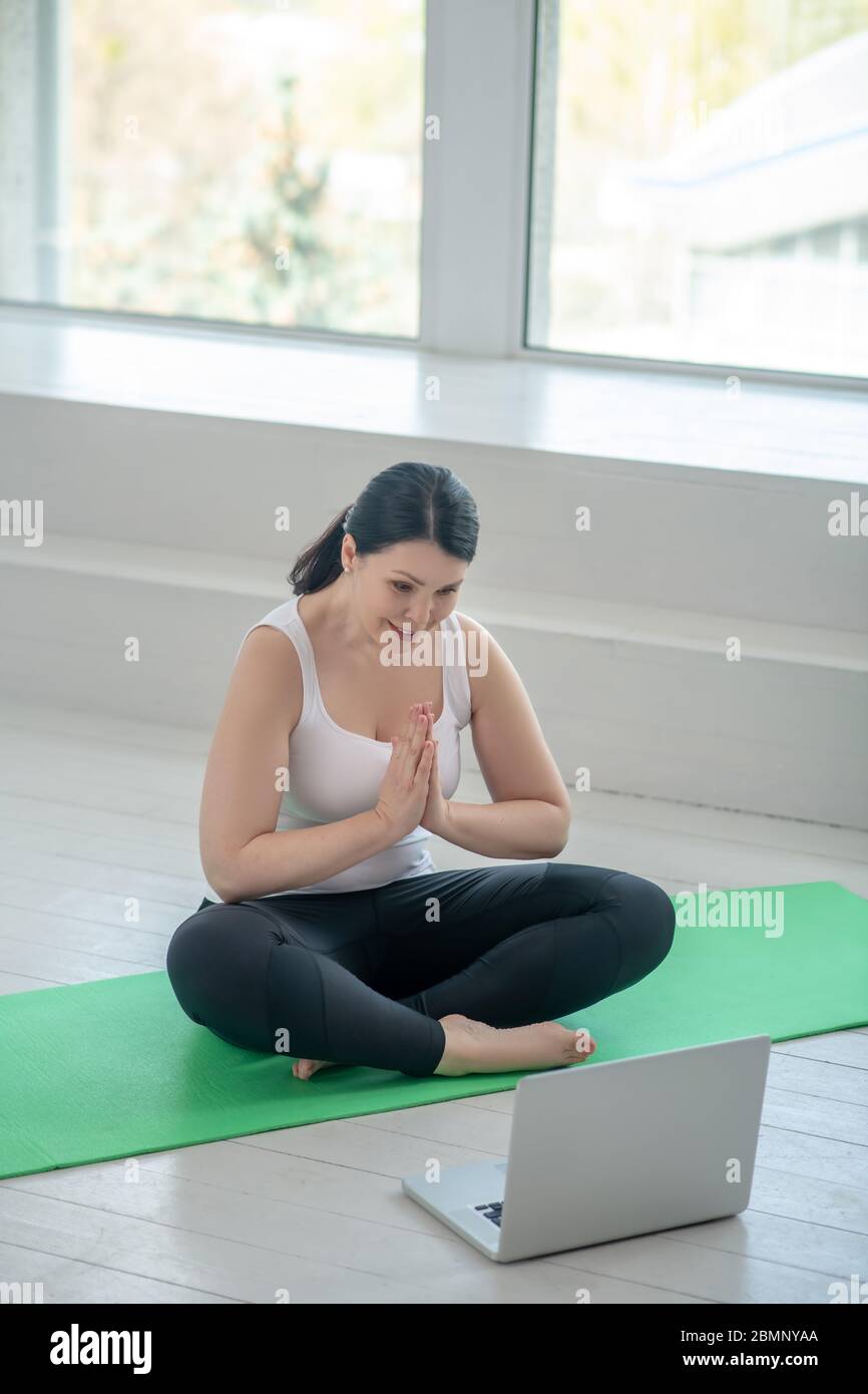 Brunette female performing namaste, having online yoga lesson, smiling ...