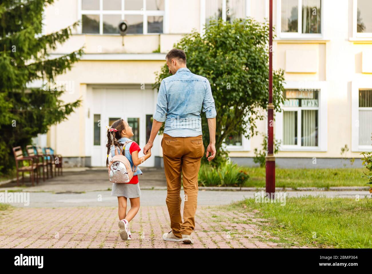 first day at school. father leads a little child school girl in first ...