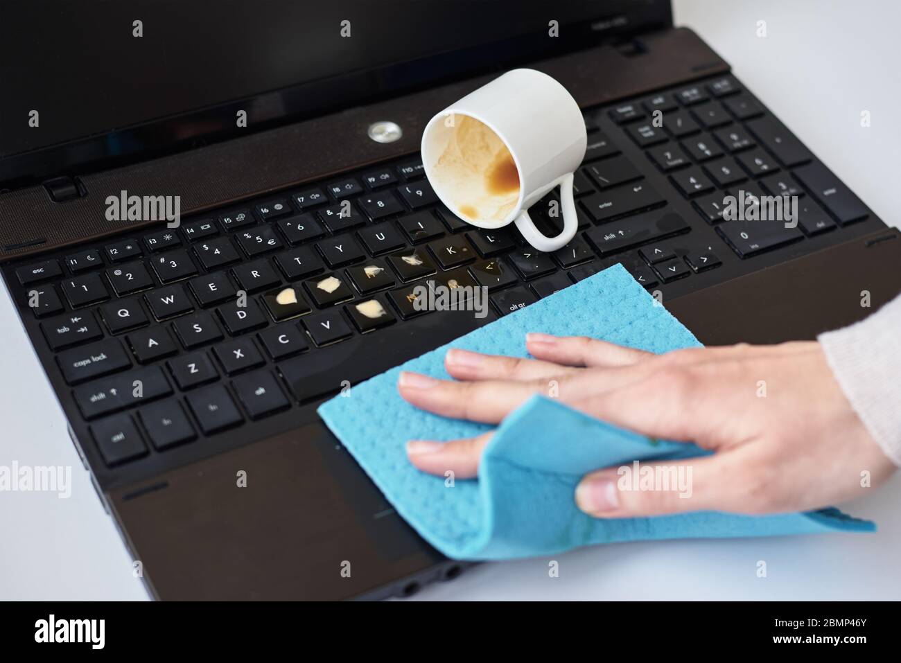 Hand cleans spilled coffee on laptop keyboard with rag Stock Photo - Alamy