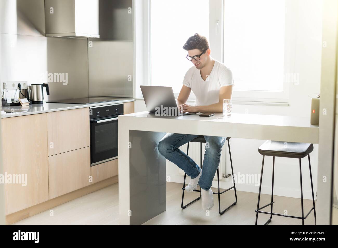 Man in kitchen using laptop smiling Stock Photo - Alamy