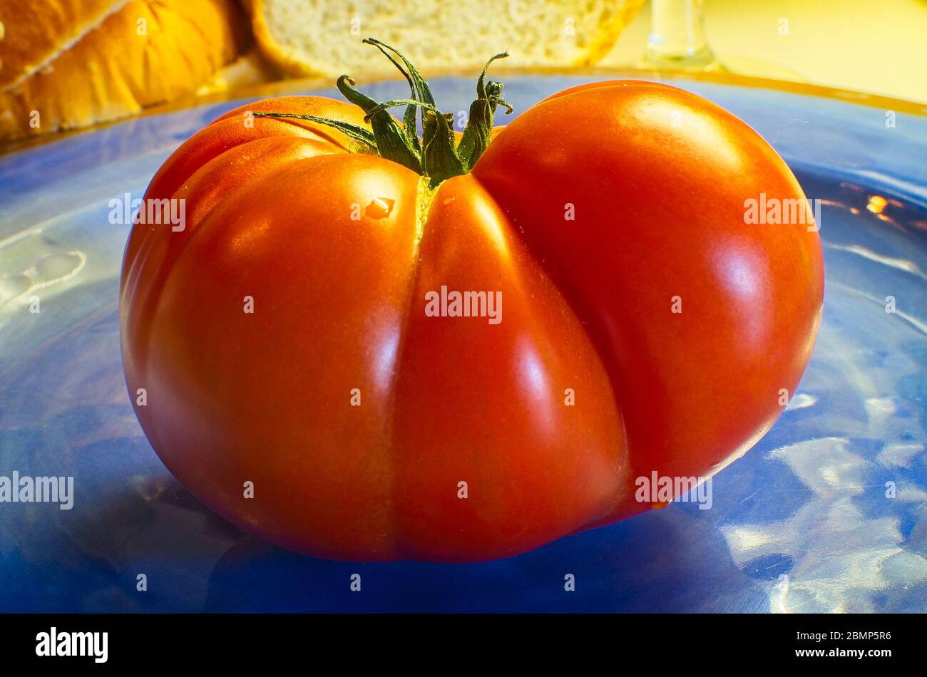 Red raf tomato on blue plate. Fresh food Stock Photo - Alamy