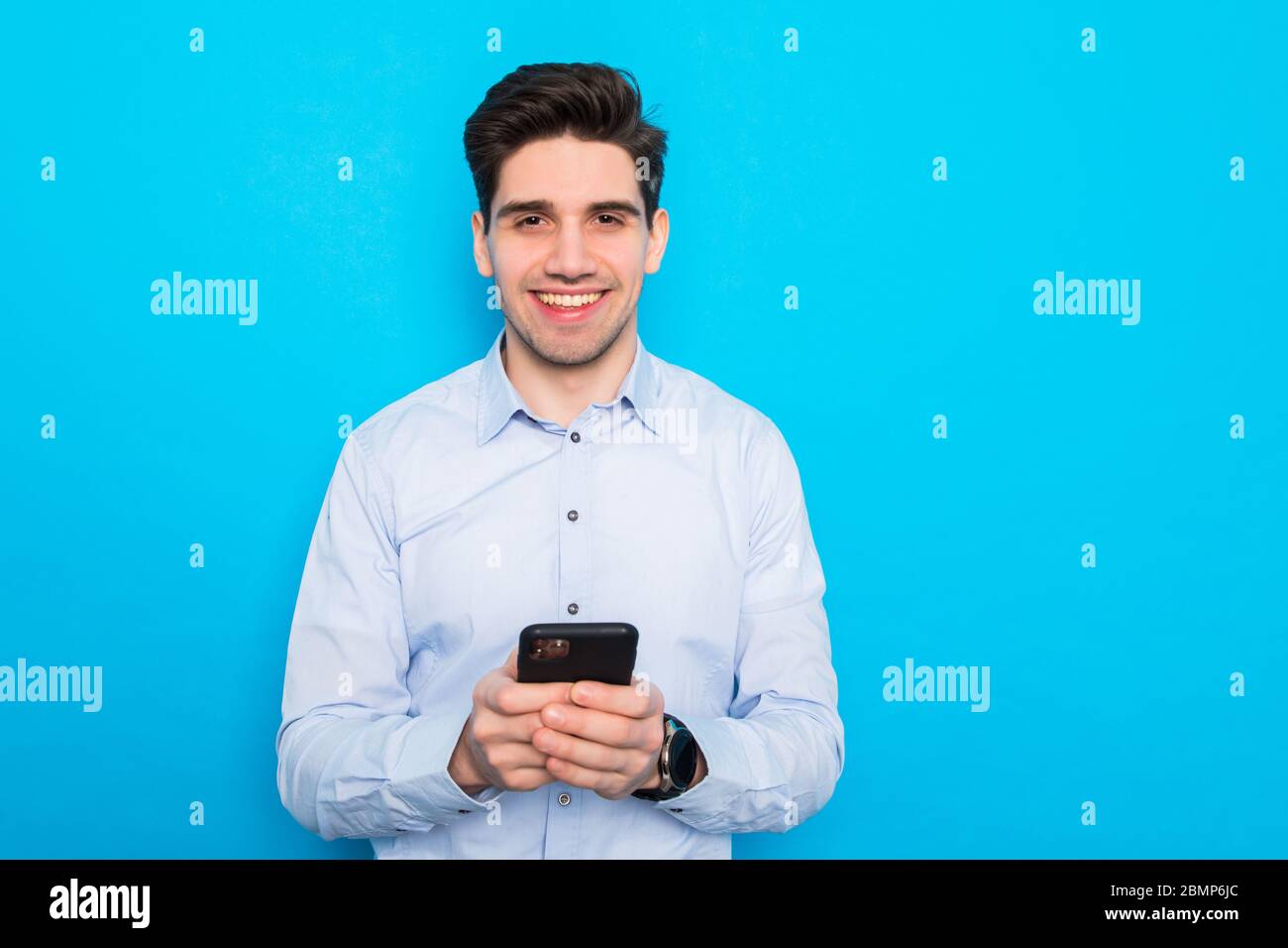 Smiling young man holding mobile phone, looking at screen isolated on ...