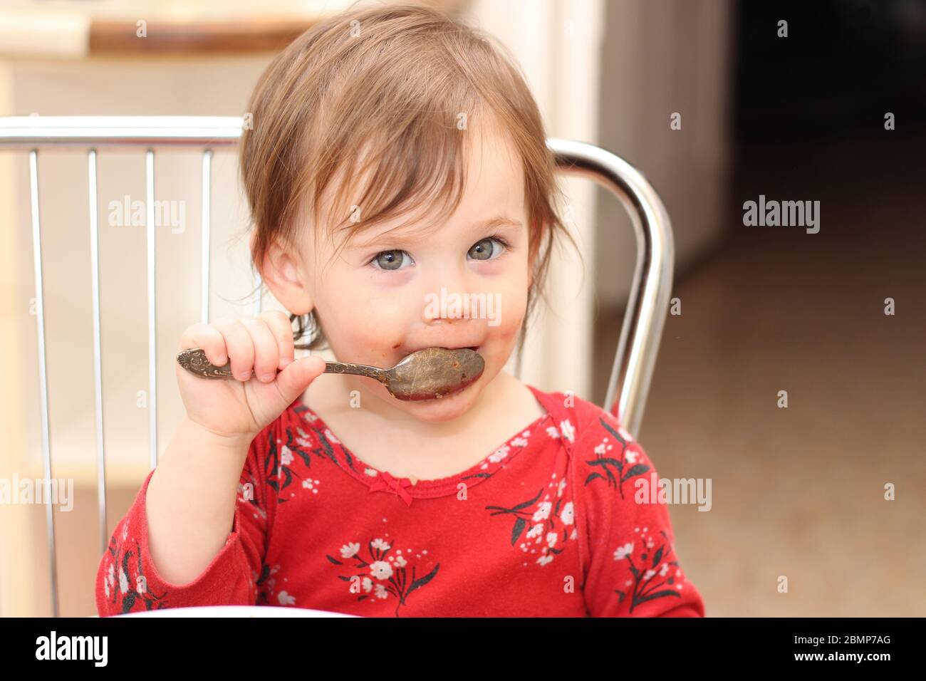 Little white dirty child eats with a spoon in the kitchen sitting on a chair Stock Photo - Alamy