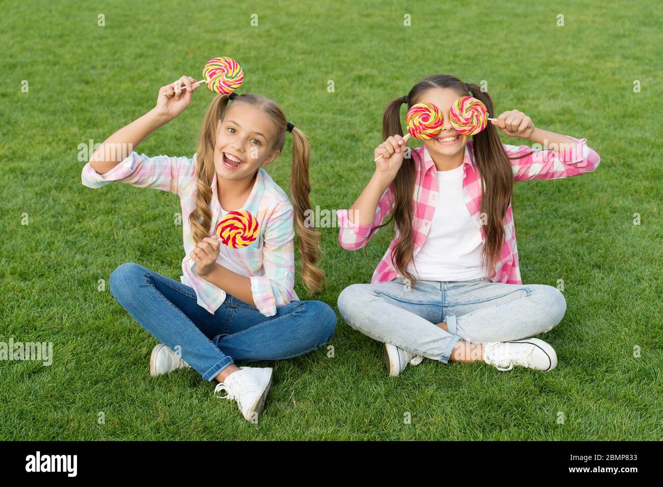 Sweet childhood. Happy children hold candy sit green grass. Candy shop ...
