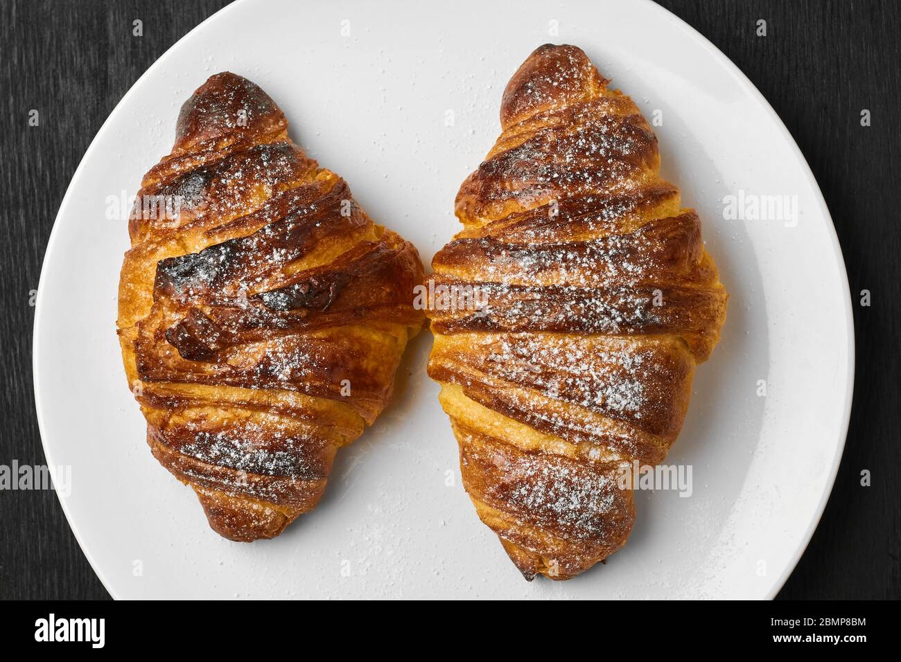 Flat lay of two buttery croissants on a white plate on a black ...