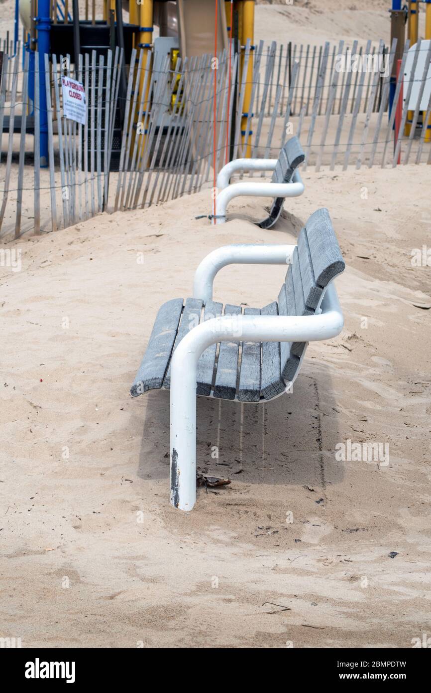 A closed beach almost covers wooden park benches, by a fenced in ...