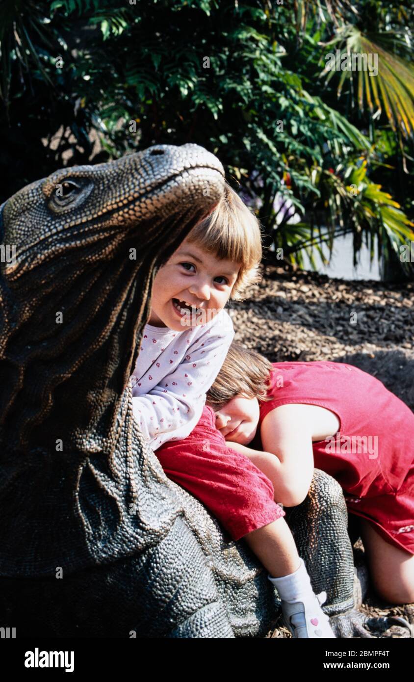 Two young children / girls sitting and playing on a large brass lizard ...