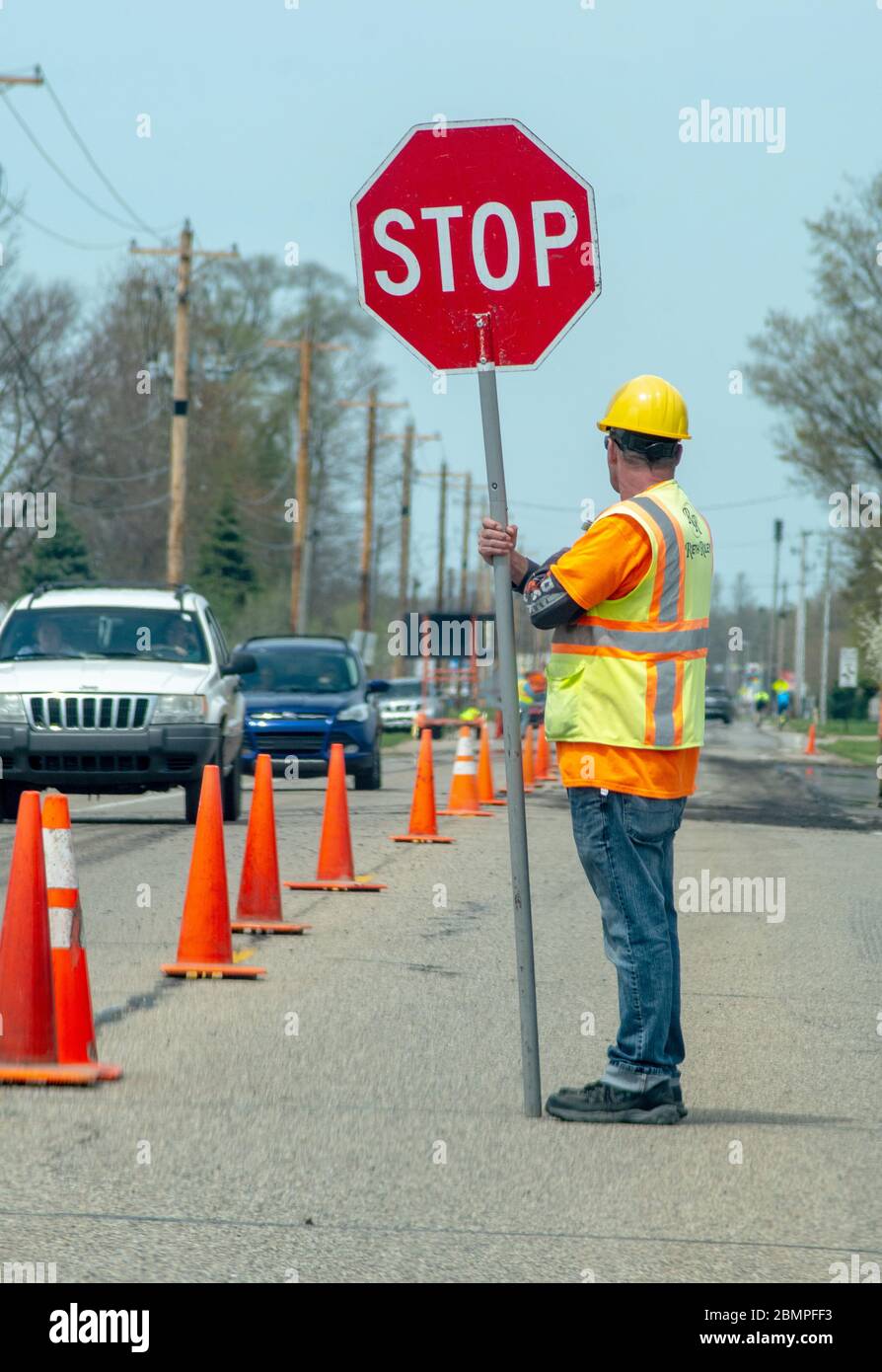 Road worker holds stop sign to direct traffic while a crew repairs a ...