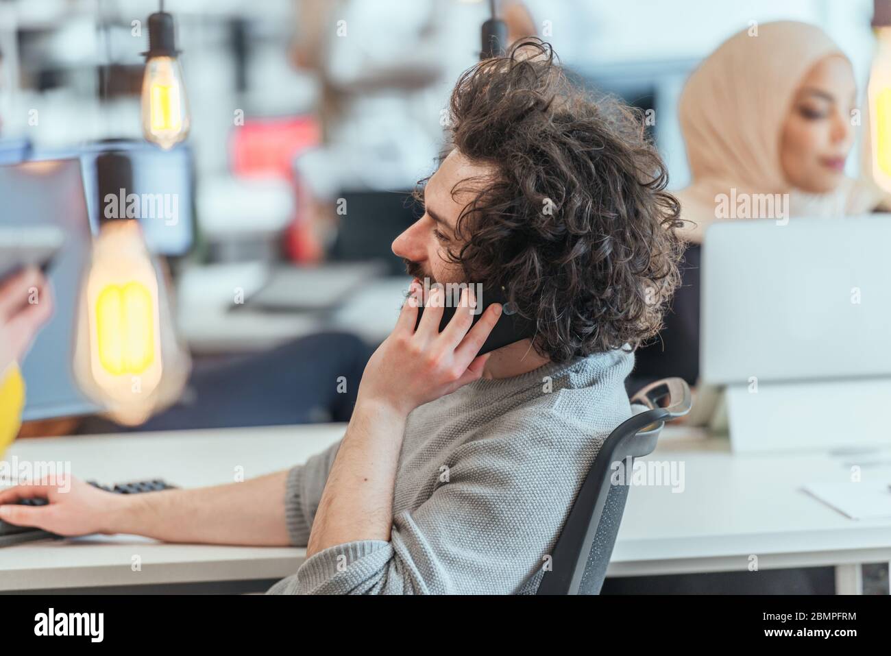 Bearded employee guy with afro haircut talking on his phone while being ...