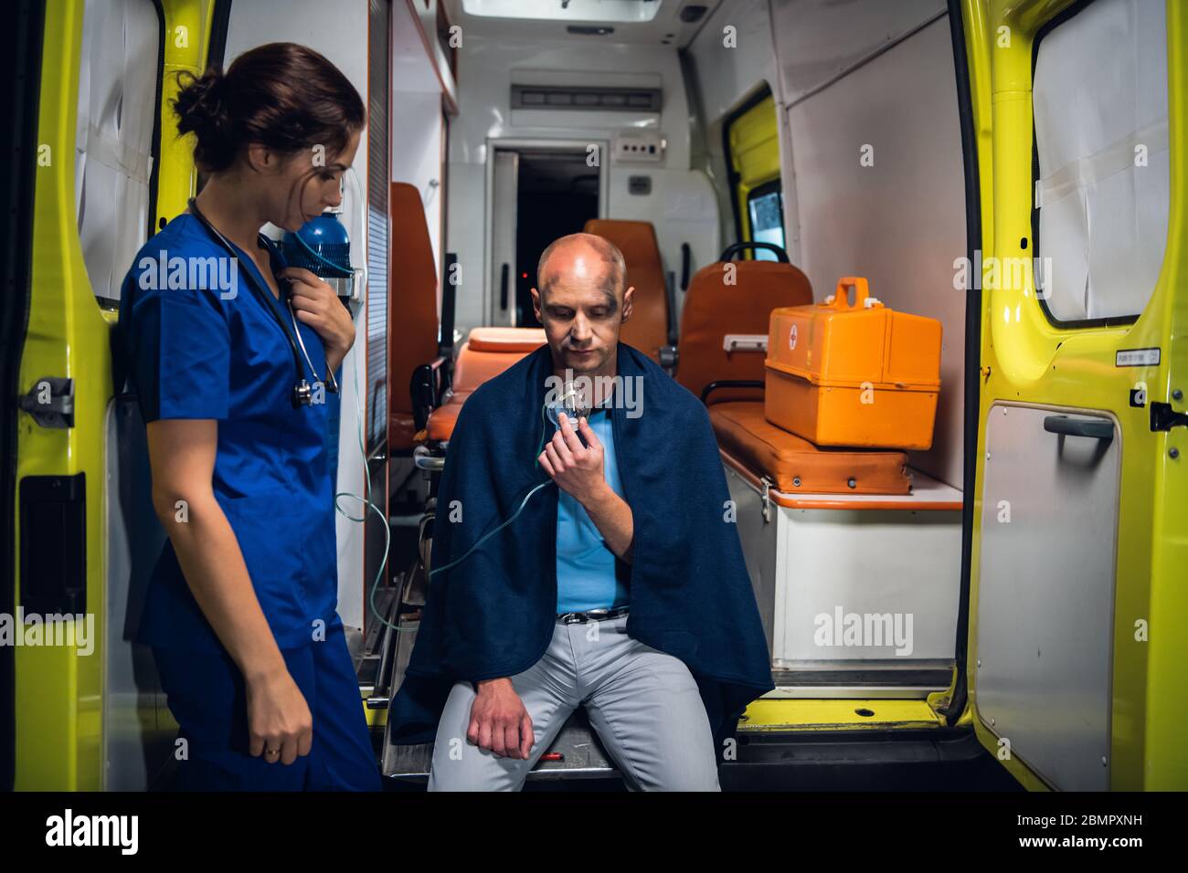 Ambulance car, a young nurse is giving an oxygen mask to an injured man ...