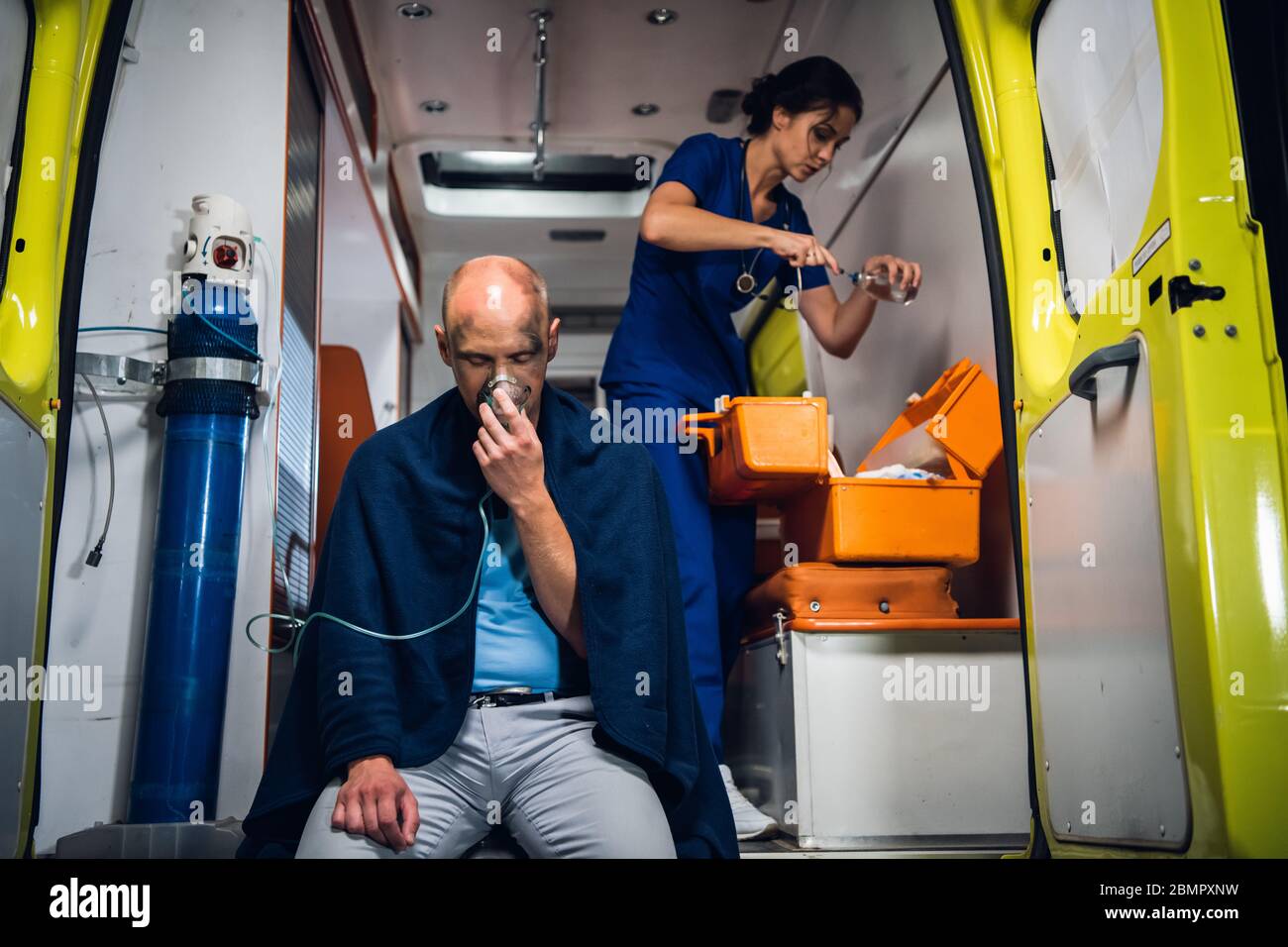 Rescued man is sitting in an ambulance car, young nurse is preparing ...