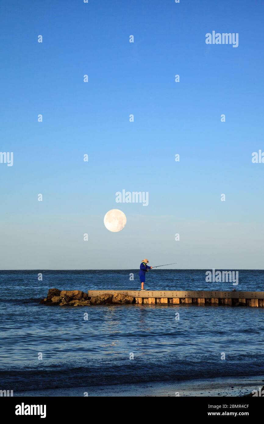 Fisherman on the jetty as the full moon sets over the ocean in Miami ...