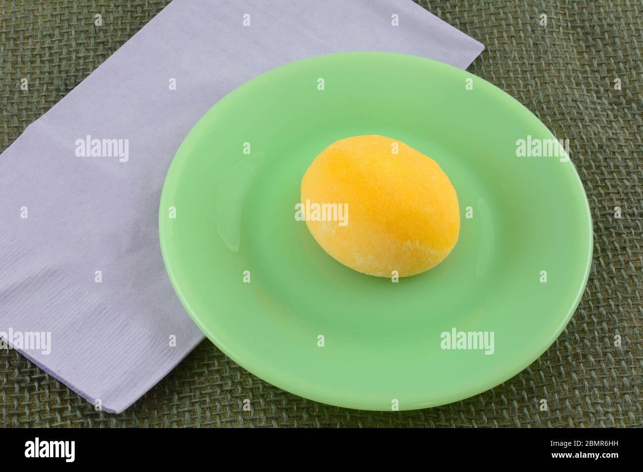 Mango ice cream mochi ball on green dessert plate with lavender napkin ...