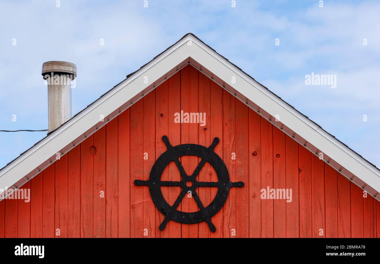 Fisherman's shack façade. Black ship’s wheel on a red-painted siding ...