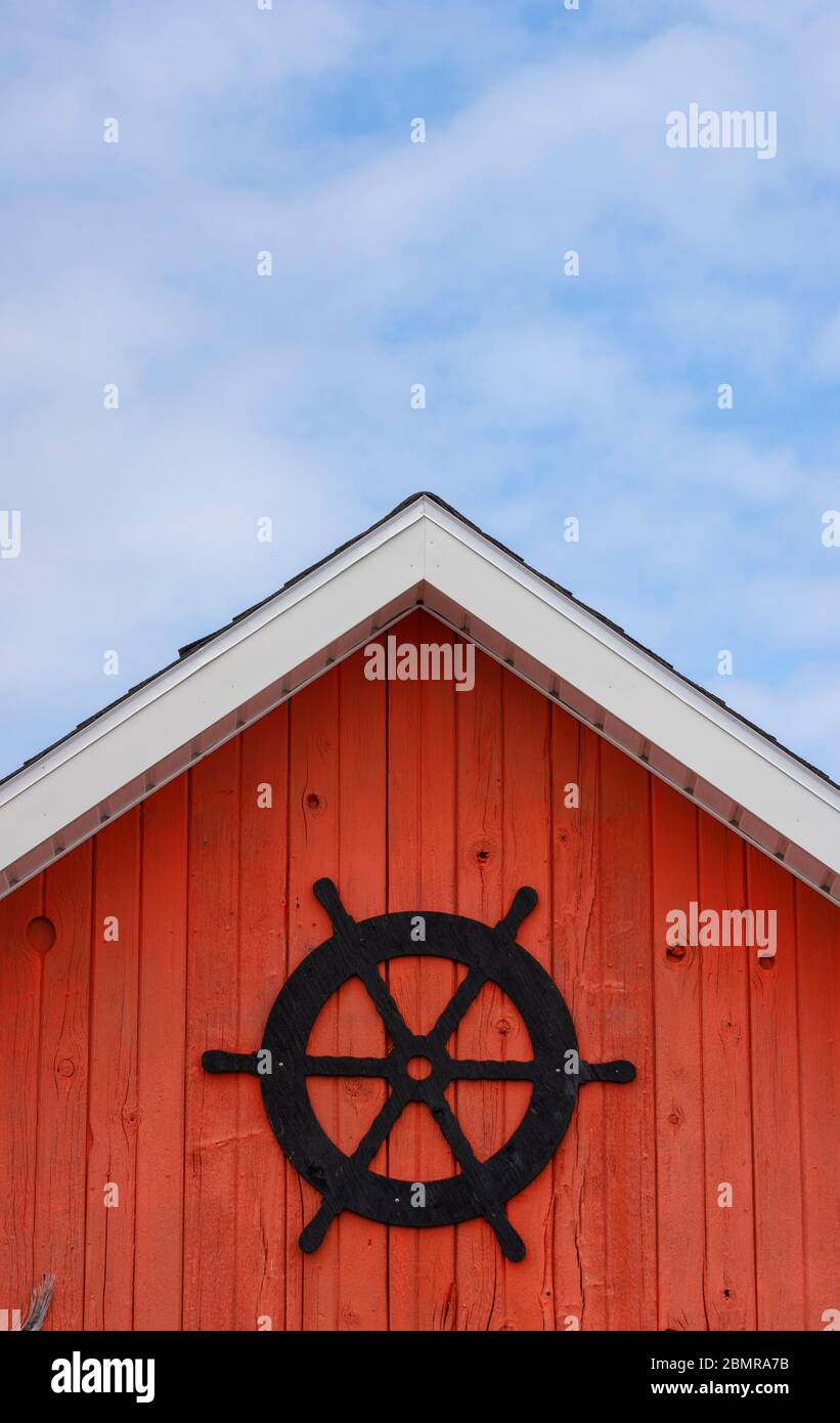Fisherman's shack façade. Black ship’s wheel on a red-painted siding ...